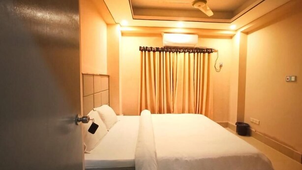 Quarto de hotel com cama, ventoinha no teto, mesa de cabeceira e janela com cortinas.