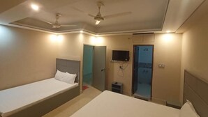 Quarto de hotel com duas camas, ventoinha no teto, iluminação embutida, televisão e uma mesa pequena.
