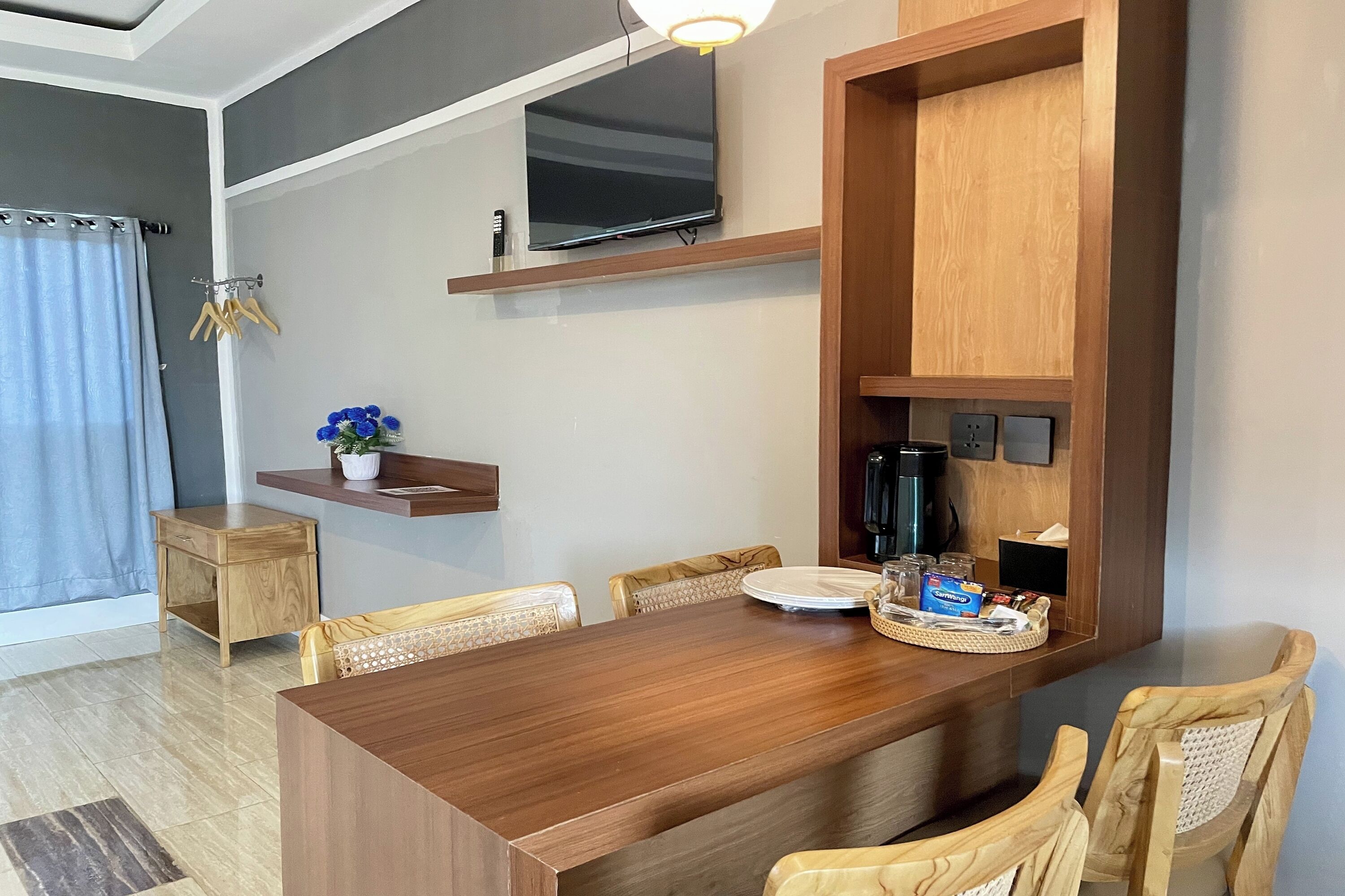 Uma área de refeições moderna com uma mesa de madeira, cadeiras, uma TV presa à parede e uma pequena estante com objetos.