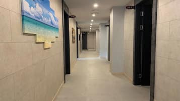 Um corredor de hotel com portas numeradas, chão de azulejos e um quadro com uma praia.