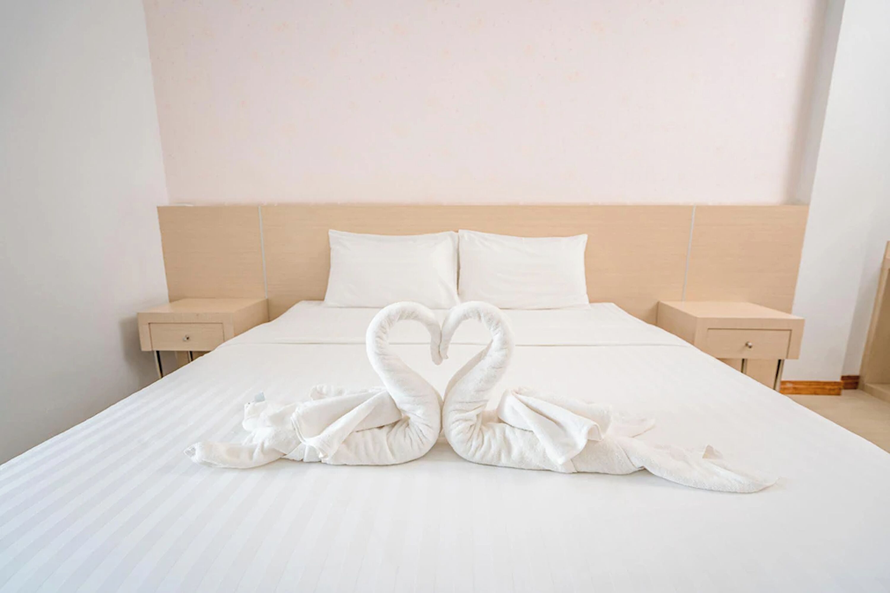 Quarto de hotel com uma cama grande, duas mesas de cabeceira e uma decoração de toalha em formato de coração na cama.