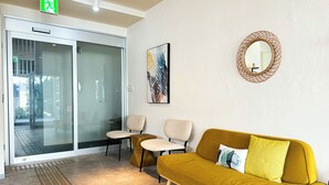 Uma área de recepção com um sofá amarelo, duas cadeiras, uma obra de arte emoldurada e um espelho redondo na parede.