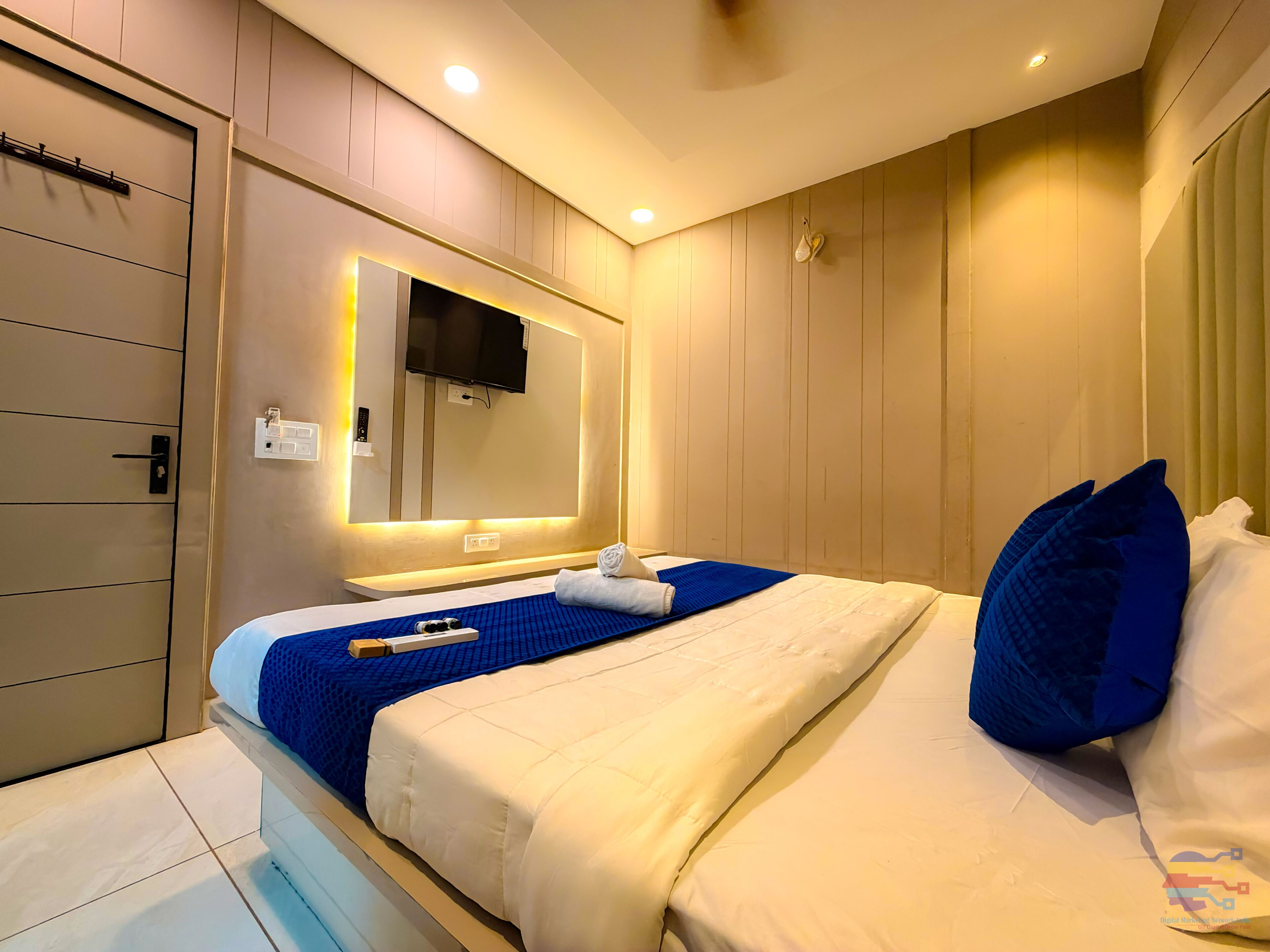 Quarto de hotel com uma cama, televisão, espelho e mesa de cabeceira.