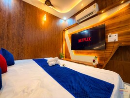 Quarto de hotel com uma cama grande, televisão de tela plana, painéis de madeira e ar condicionado.