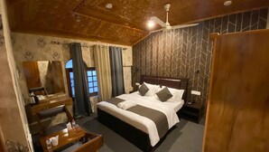 Quarto com uma cama grande, uma escrivaninha de madeira, um espelho e um ventilador de teto.