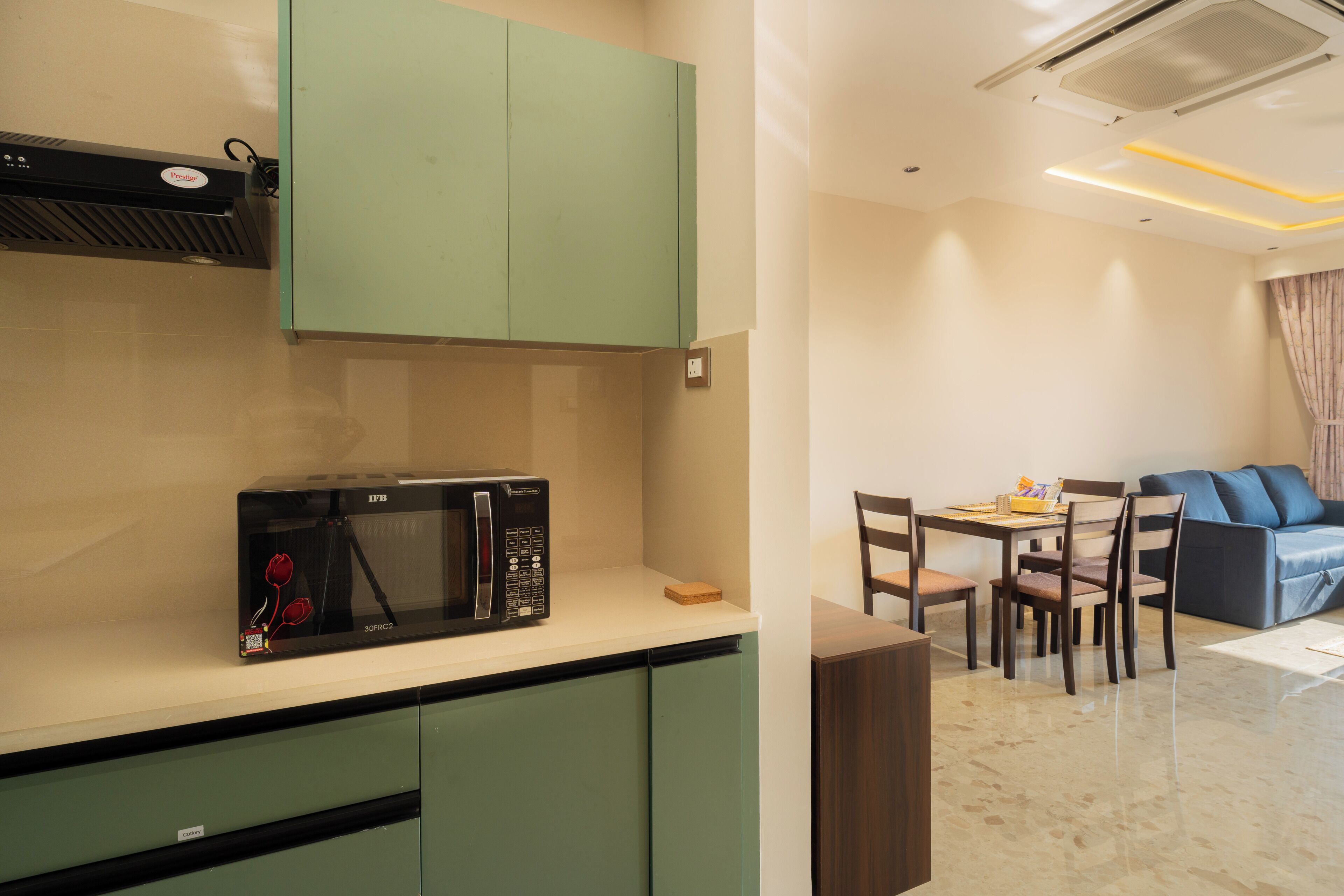 Cozinha compacta com micro-ondas, área de refeições com mesa e cadeiras, e sala de estar com sofá.