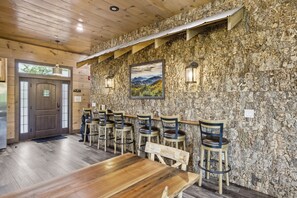 Um interior rústico com parede de pedra, teto de madeira e uma área de jantar com cadeiras e mesa.