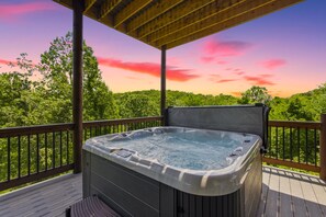 Uma banheira de hidromassagem em um deck de madeira com vista para árvores e um pôr do sol.