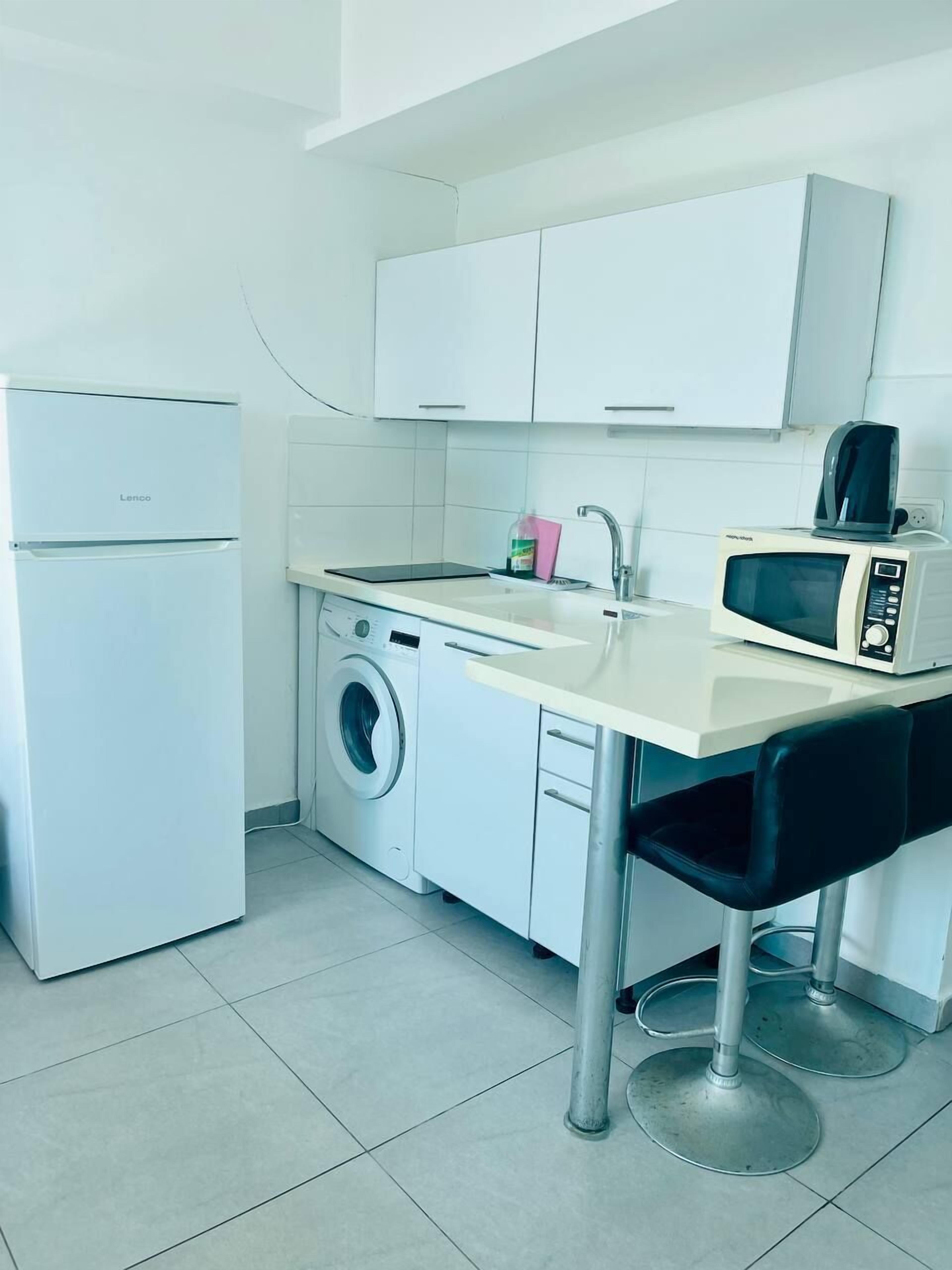 Uma cozinha compacta com máquina de lavar, micro-ondas e pia.
