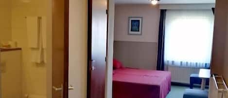 Quarto de hotel com banheiro, cama, escrivaninha e janela.