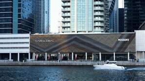 Um edifício moderno com a sinalização 'DARGLO GLOBAL' e 'MISSONI', situado à beira-mar, com um barco em movimento.