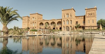 Um edifício grande e tradicional com janelas arqueadas e um pátio com piscina refletora.