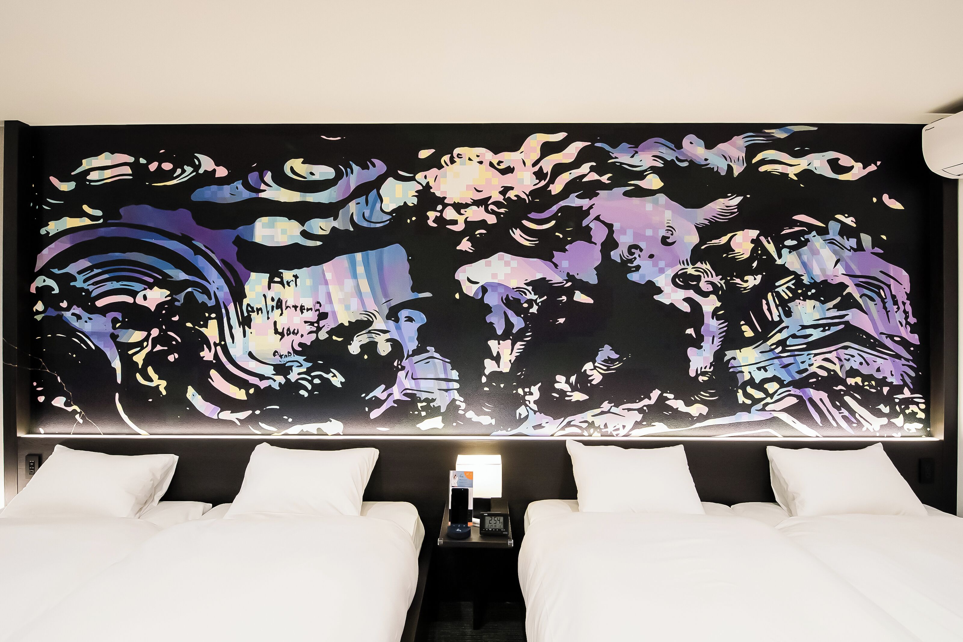 Quarto de hotel com duas camas, uma grande obra de arte abstrata na parede e uma mesa de cabeceira com abajur e telefone.