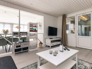 Uma sala moderna com televisão de tela plana, espaço de jantar com mesa e cadeiras, e cozinha com fogão e armários.