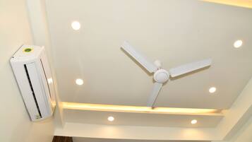 Ventilador de teto com luminária e iluminação embutida em um quarto com paredes brancas e piso de madeira.