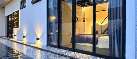 Quarto de hotel moderno com uma grande porta de vidro deslizante, uma cama e banheiro visível.