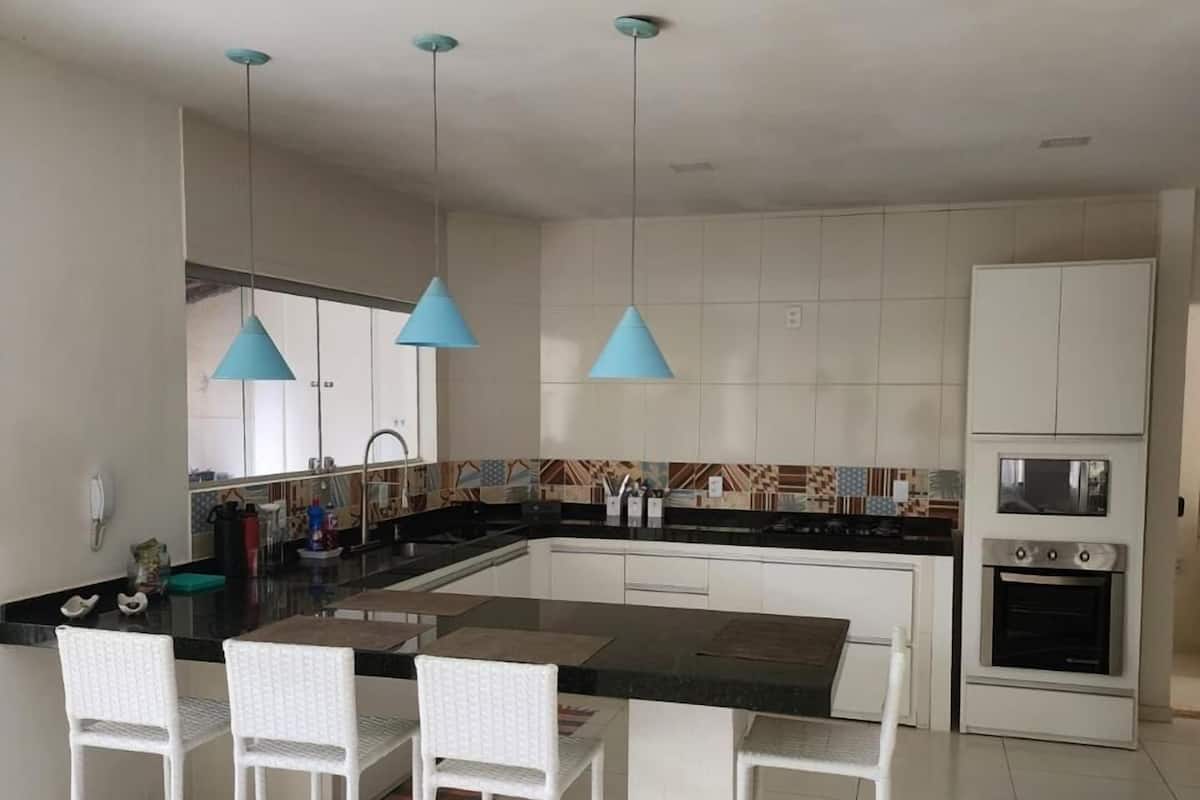 Uma cozinha moderna com armários brancos, bancada preta e três luminárias pendentes azuis.