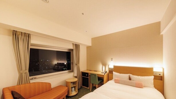 Quarto de hotel com cama, sofá, escrivaninha e janela com cortinas.