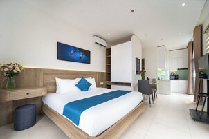 Quarto de hotel moderno com uma cama grande, escrivaninha, cadeira, pequena cozinha e televisão.