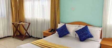 Quarto de hotel com uma cama, mesa de cabeceira com telefone e janela com cortinas.