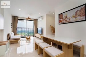 Uma sala de estar moderna com sofá, mesa de jantar com bancos, TV e uma grande janela com vista.
