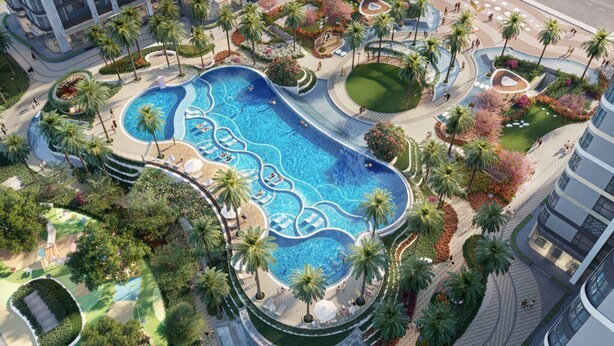 Uma piscina grande e sinuosa cercada por palmeiras e áreas ajardinadas, com edifícios modernos ao fundo.