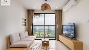 Uma sala de estar moderna com um sofá, uma mesa de centro, uma televisão sobre um console de madeira e uma janela grande com vista.