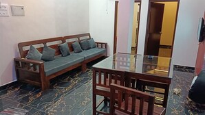 Um quarto com sofá de madeira, mesa de jantar com tampo de vidro e uma cadeira de madeira.