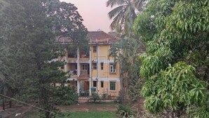Um edifício com várias andares e fachada amarela, cercado por vegetação densa e árvores.