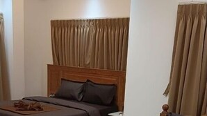 Quarto de hotel com duas camas, cabeceiras de madeira, piso de mármore e teto com iluminação embutida.