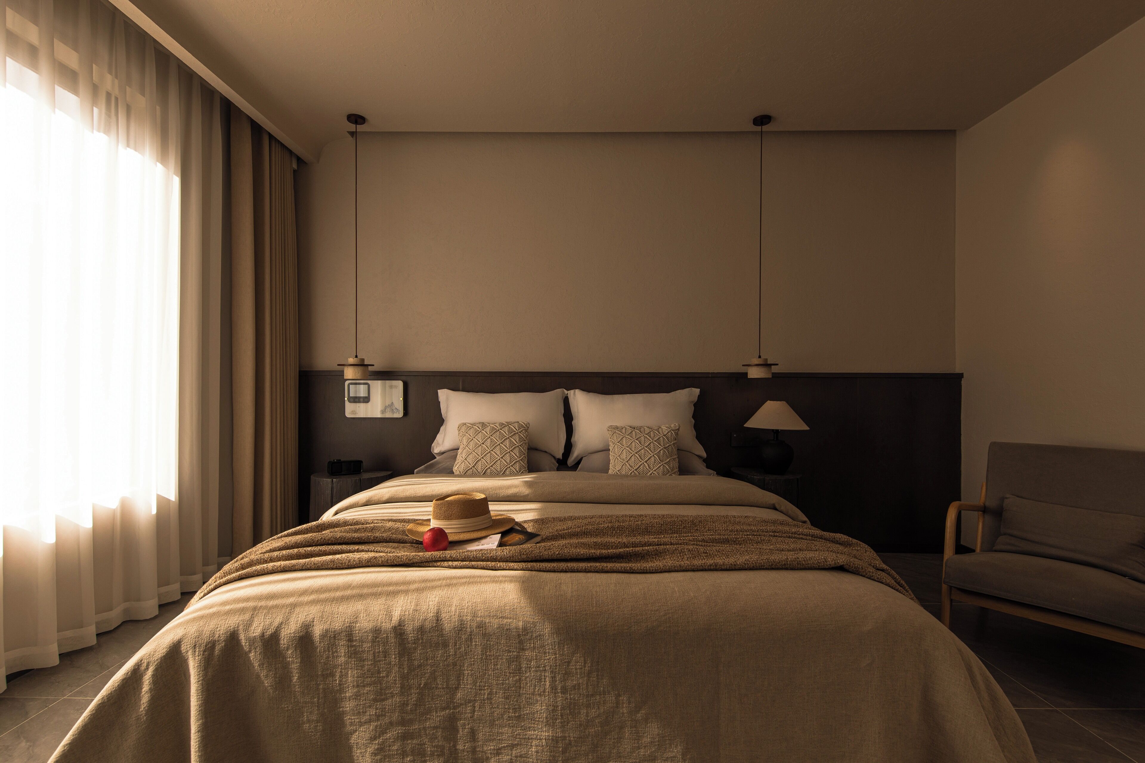 Quarto de hotel moderno com uma cama grande, uma mesa de cabeceira, uma luminária e uma cadeira.