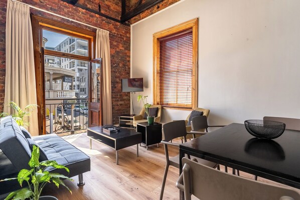 Uma sala de estar moderna com sofá, mesa de jantar, cadeiras, TV e varanda com vista para um prédio.