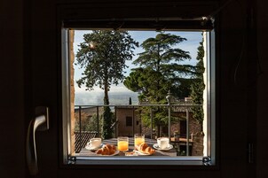 Disposição para o café da manhã com croissants, suco de laranja e café numa varanda com vista panorâmica para árvores e uma paisagem distante.
