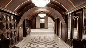 Um corredor com piso estampado, painéis de madeira e um candelabro.