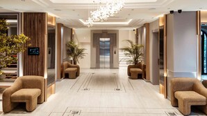 Um hall de hotel moderno com um candelabro, assentos e um painel digital.
