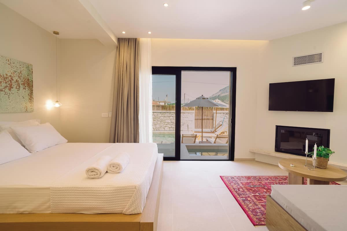 Quarto de hotel moderno com uma cama grande, televisão de tela plana, varanda com assento externo e vista para as montanhas.