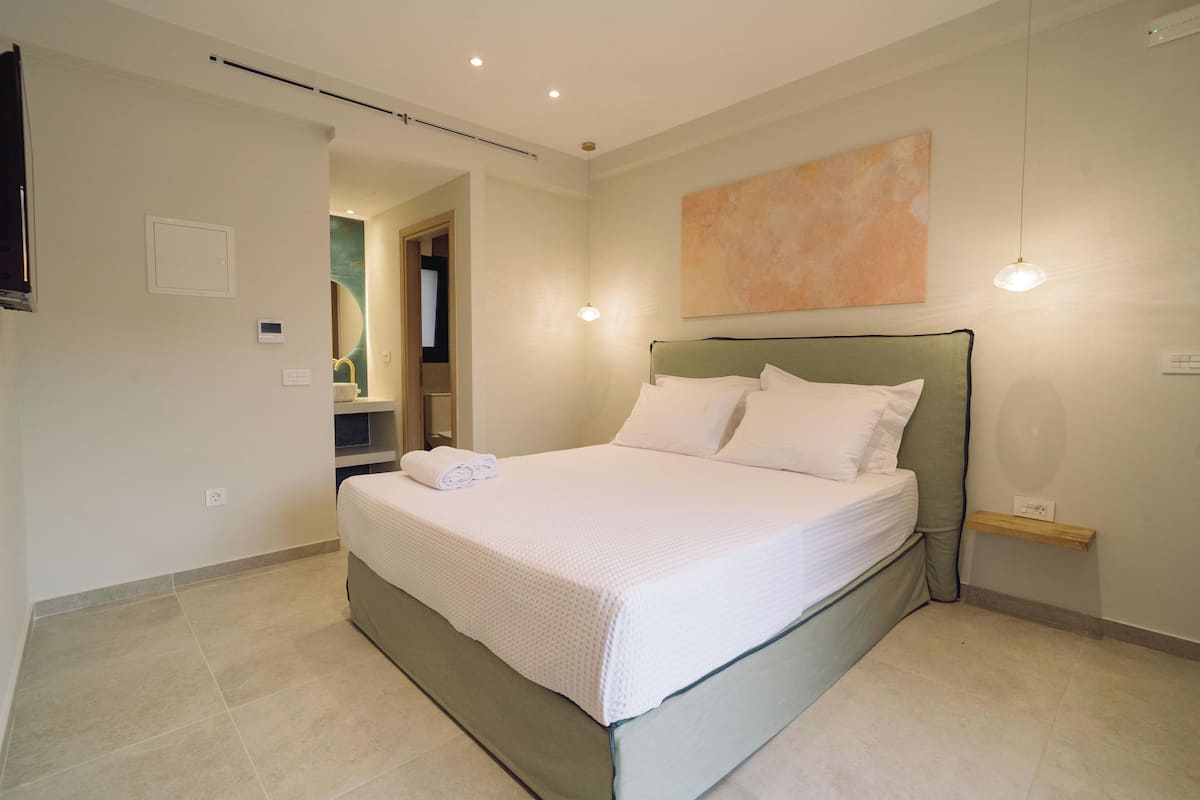 Quarto moderno com cama, mesa de cabeceira, televisão na parede e um quadro.