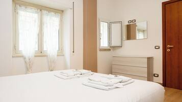 Quarto com cama, mesa de cabeceira, cômoda, espelho e janela com cortinas.