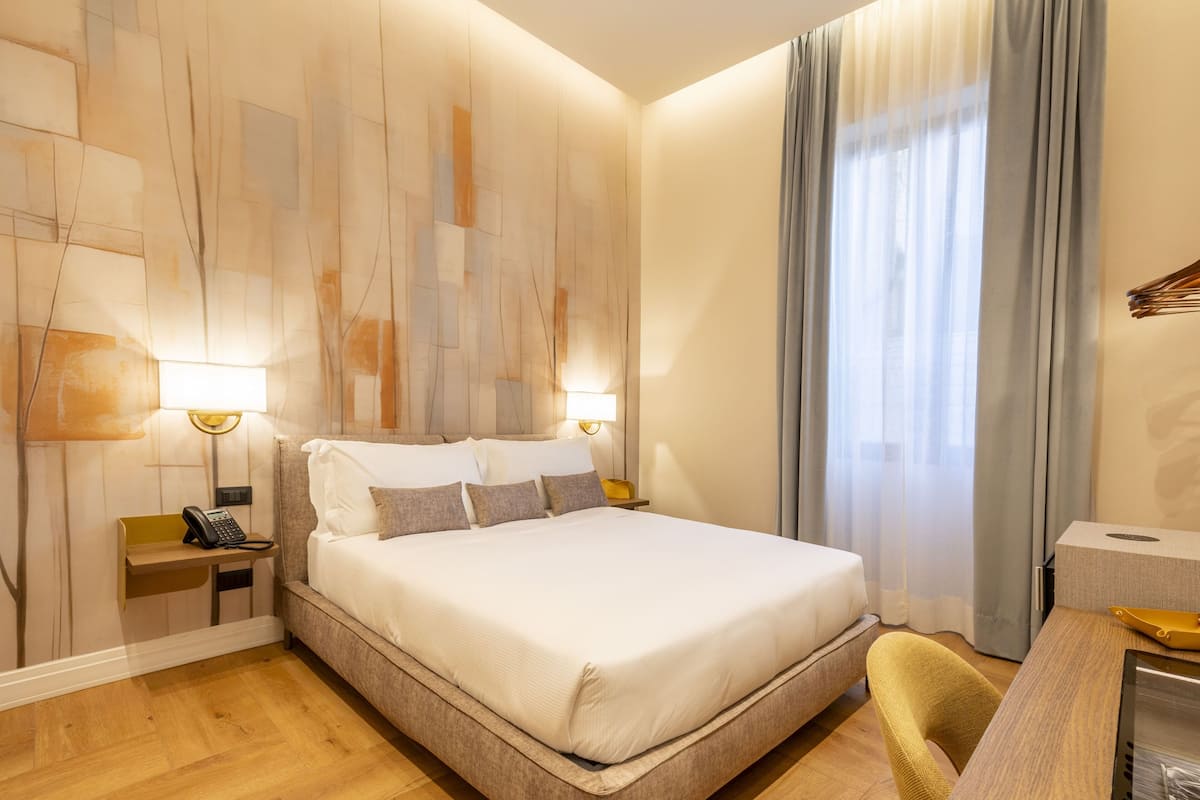 Quarto de hotel moderno com uma cama grande, luminárias de cabeceira, escrivaninha e janela com cortinas.