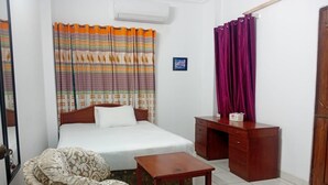 Um quarto com uma cama, uma escrivaninha, uma cadeira e uma mesinha.