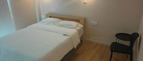 Quarto de hotel com cama, duas luminárias fixadas na parede, uma tomada e uma cadeira preta.