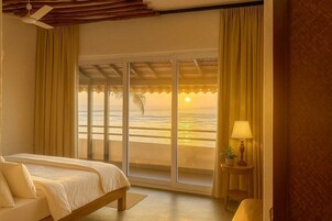 Quarto com uma cama, mesa de cabeceira com abajur e vista para o oceano ao pôr do sol.