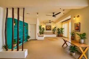 Uma sala de estar ampla com uma estante azul-esverdeada, uma mesa de centro de madeira e várias plantas em vasos.