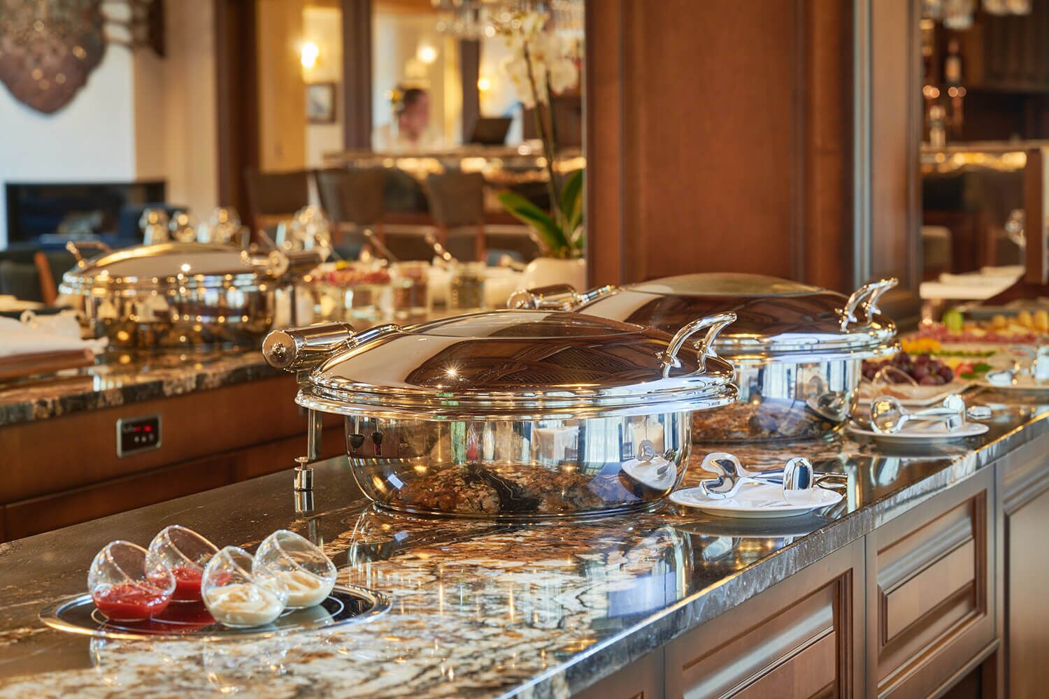 Disposição de buffet com diversos recipientes de comida e travessas sobre um balcão de mármore.