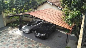 Uma garagem coberta com dois carros estacionados, um telhado em cerâmica e uma casa ao fundo.