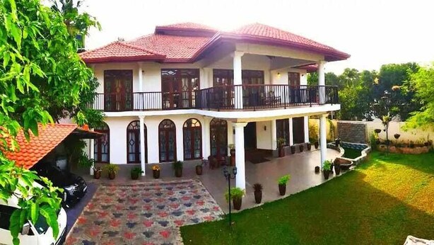 Uma casa de dois andares com varanda, alpendre coberto e gramado bem cuidado.