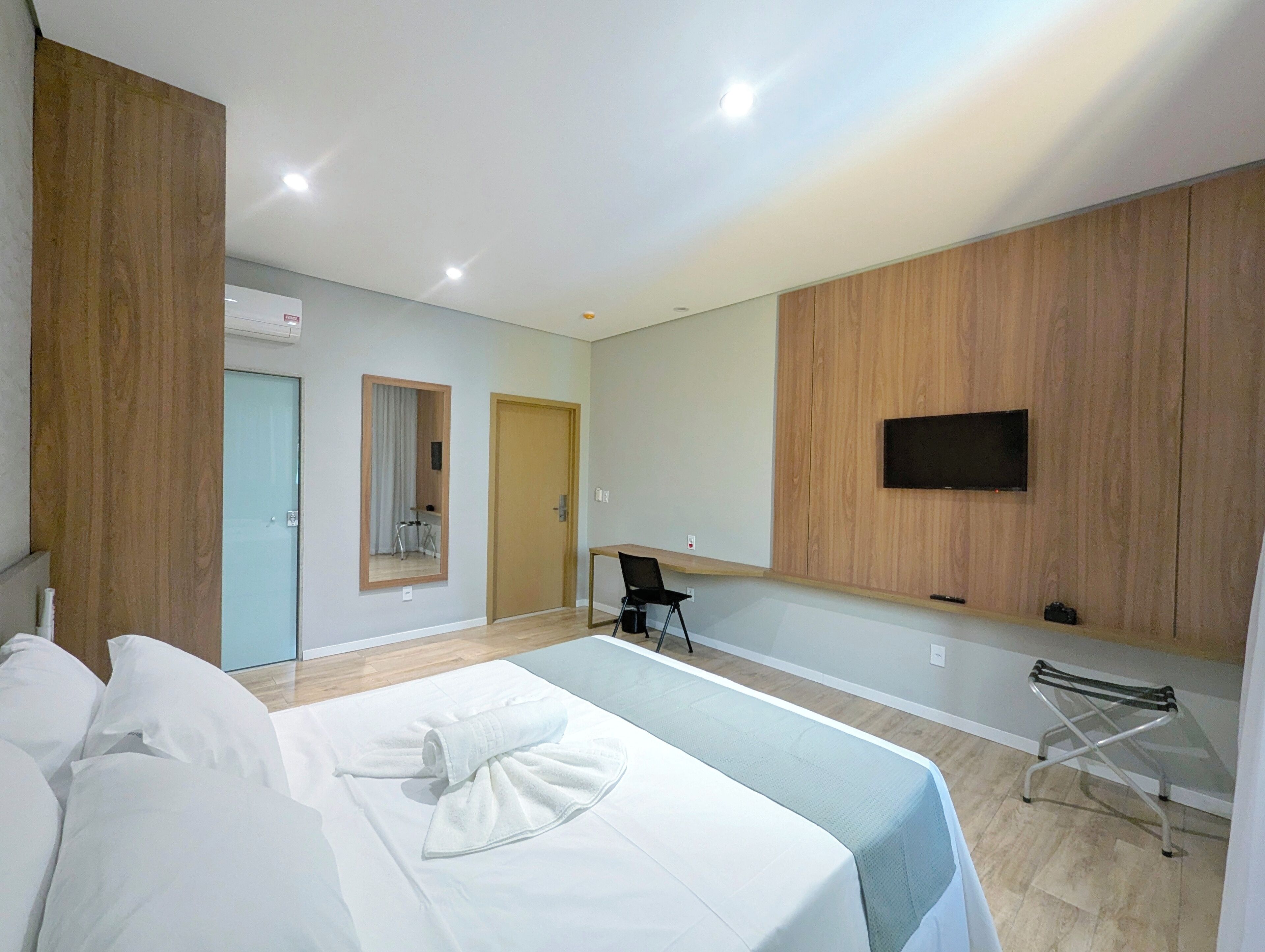 Quarto moderno com cama, escrivaninha, cadeira, televisão e espelho.