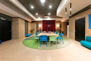 Uma sala de reuniões moderna com uma mesa comprida, várias cadeiras e um tapete verde.