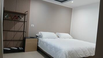 Quarto com cama, mesa de cabeceira, guarda-roupa de madeira e um cabideiro com roupas.