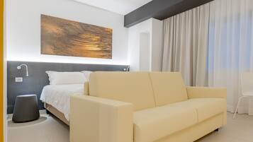 Quarto de hotel moderno com cama, sofá, obra de arte na parede e janela com cortinas.